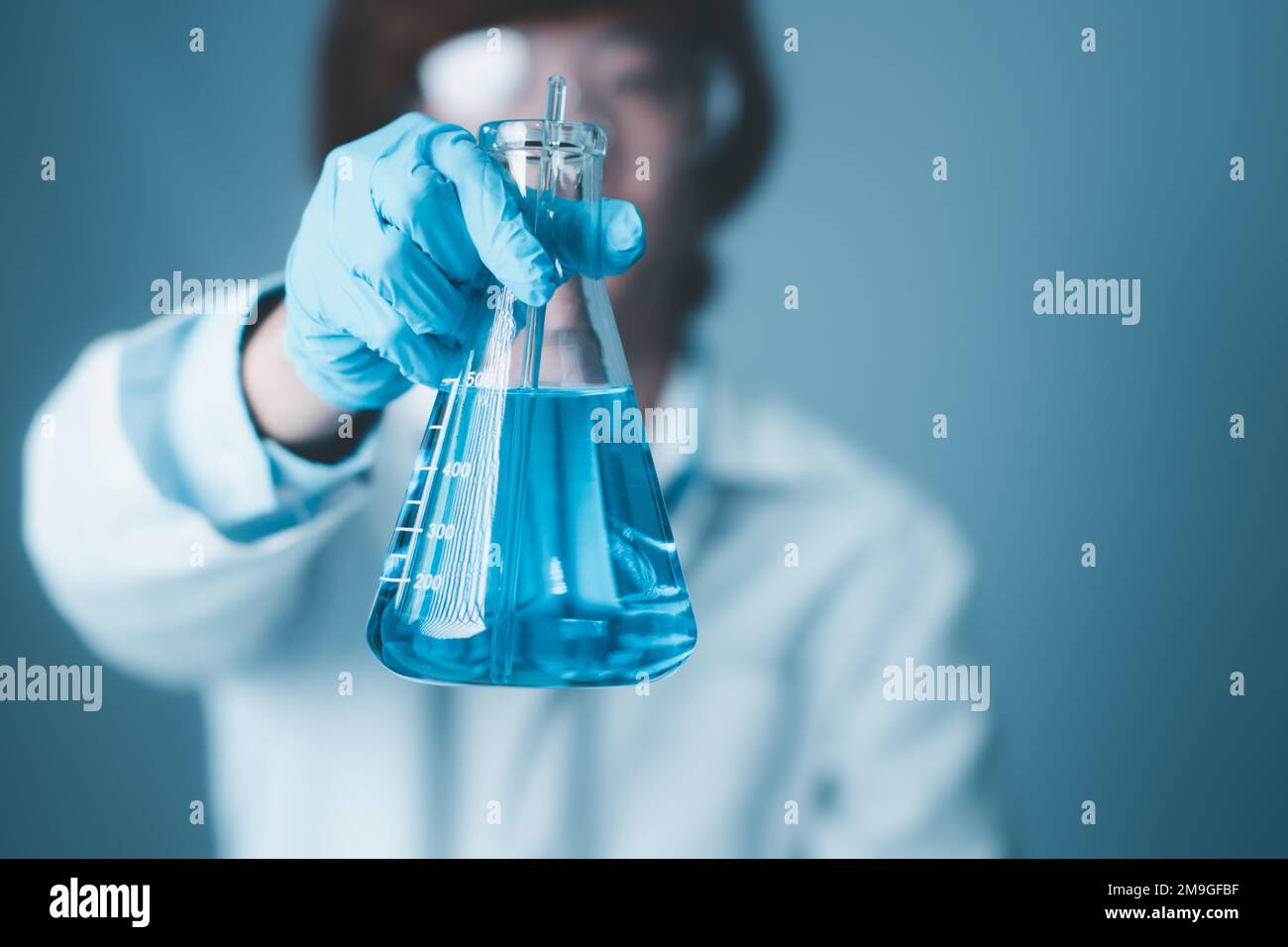 Scientist hand hold erlenmeyer flask with stirring rod filled with blue ...