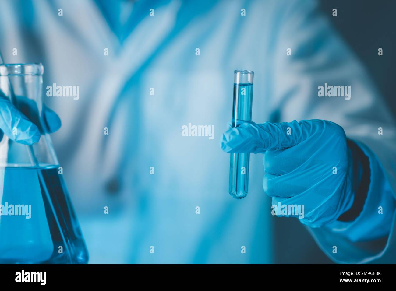 Scientist hand hold test tubes and erlenmeyer flask filled with blue ...
