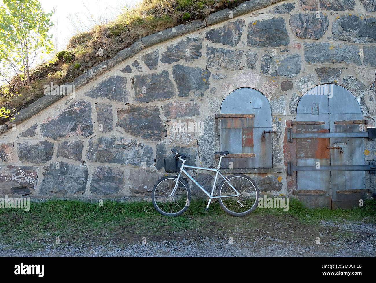 Silvercolored bicycle against old rough stone wall with two metal doors ...