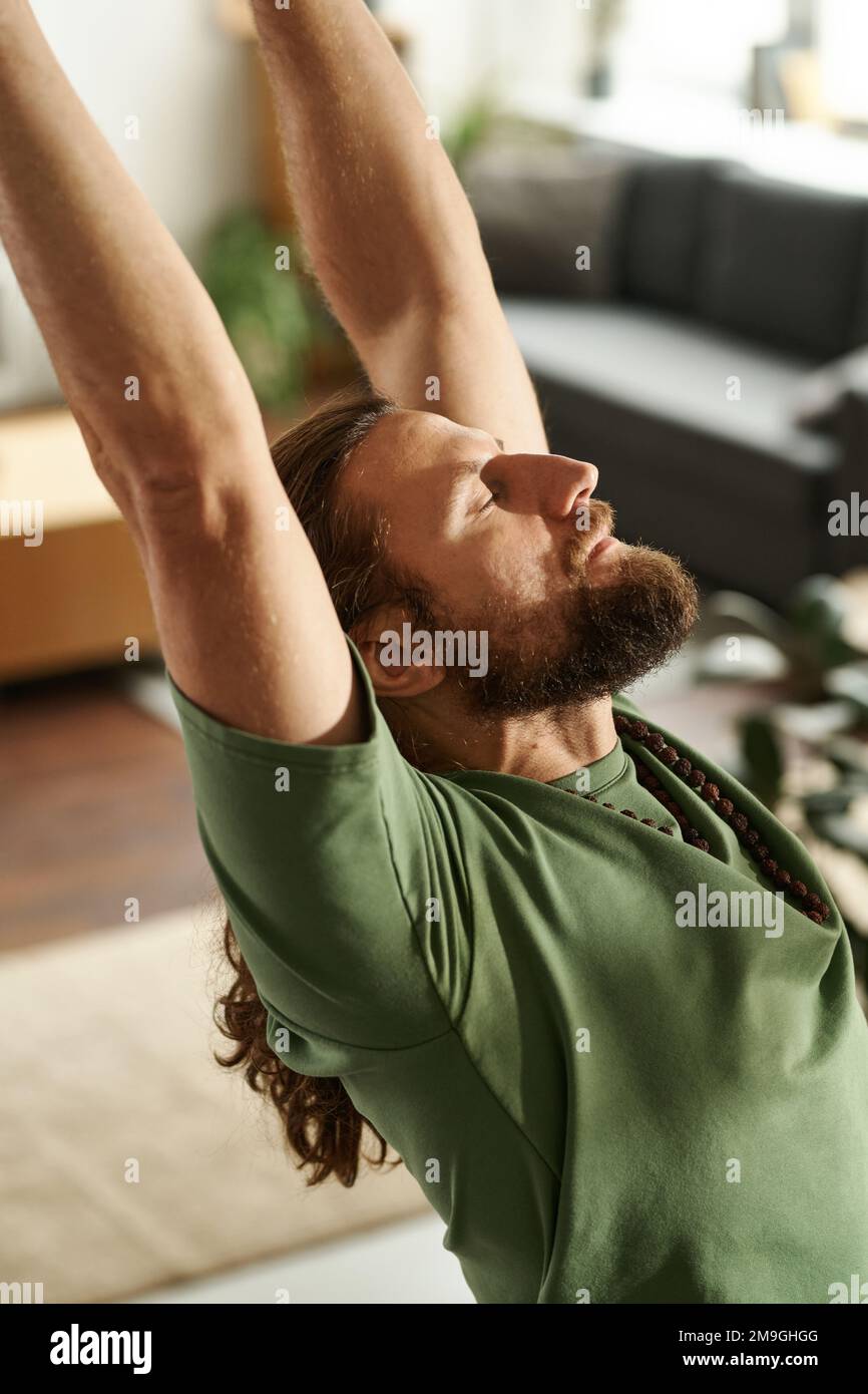 Young man raising his arms while doing stretching exercises during yoga ...