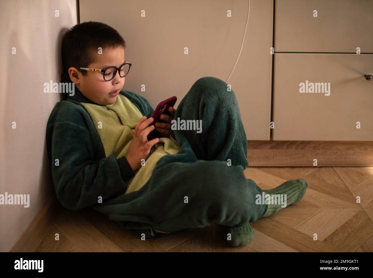 Closeup portrait of a boy who looks into the phone sitting on the floor ...