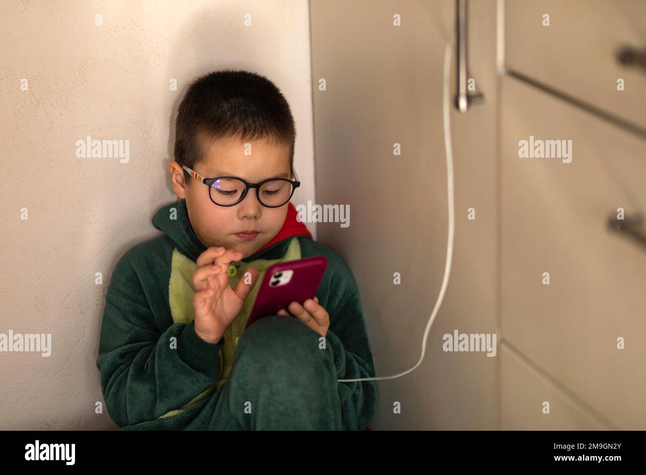 Closeup portrait of a boy who looks into the phone sitting on the floor ...