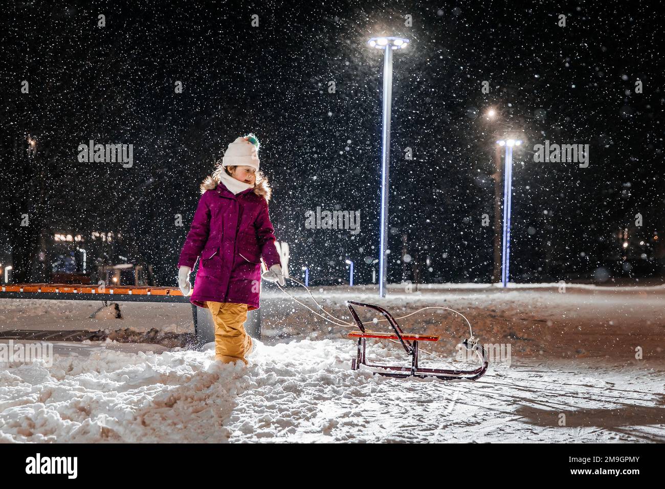 A little girl is sledding on a snowy winter evening. Falling realistic ...