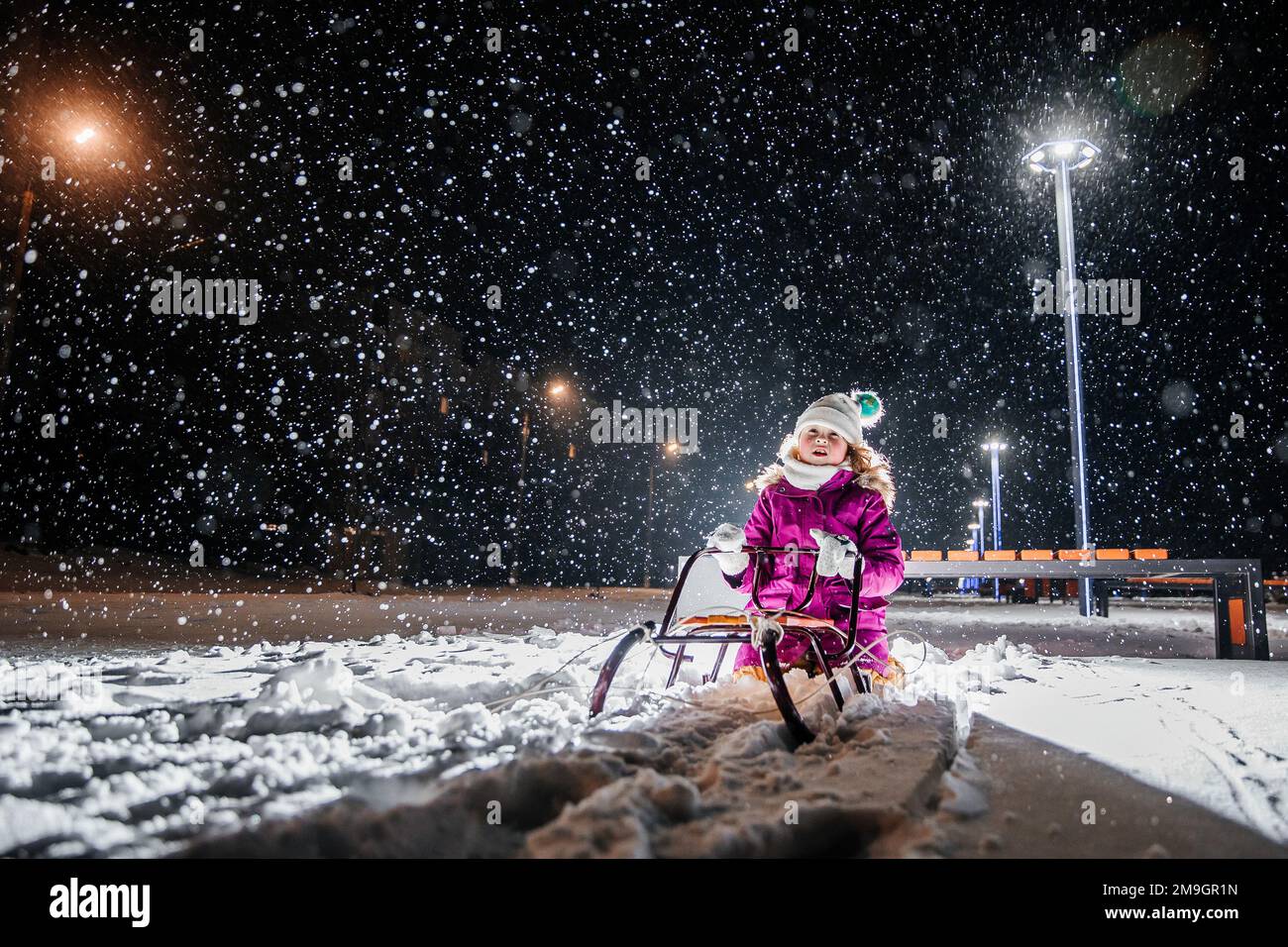 A little girl is sledding on a snowy winter evening. Falling realistic ...