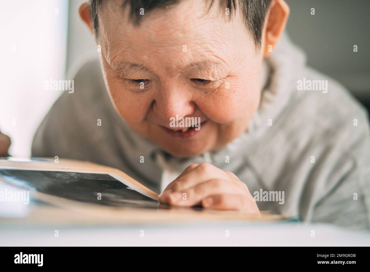 smiling elderly woman with Down syndrome looks at photos in an old ...