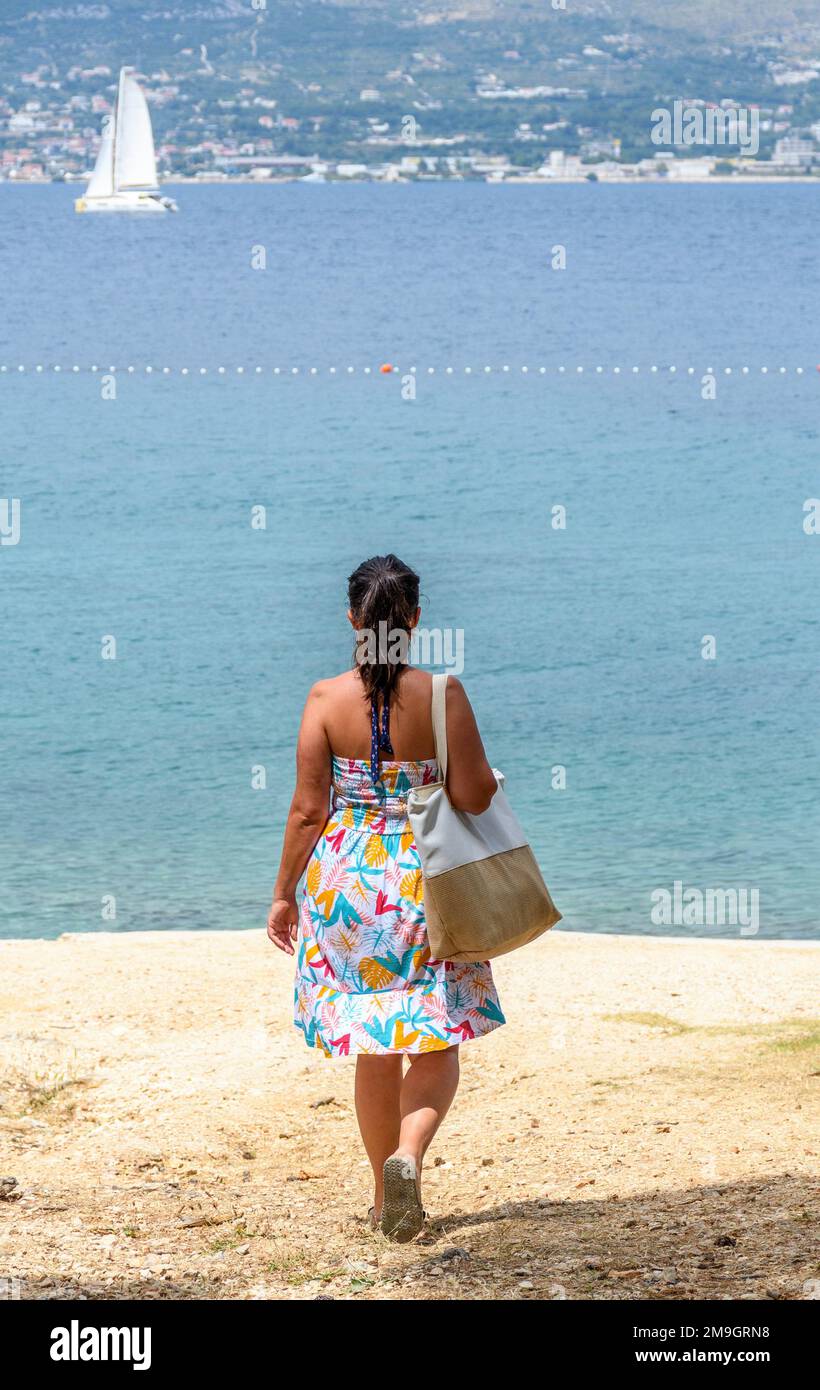 A back view of a young female walking on Bene beach in Split, Croatia ...
