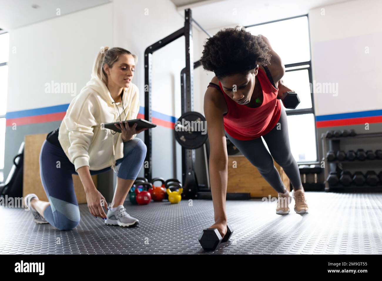 African american fit woman doing push ups with dumbbells with caucasian ...