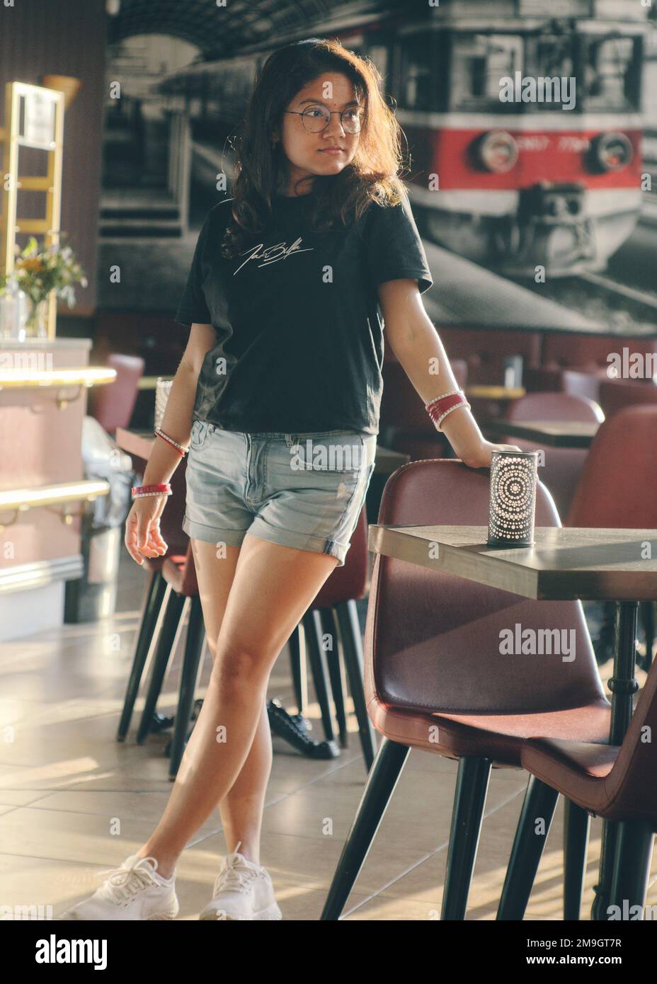 A vertical shot of a young female in a summer outfit posing in a cafe ...