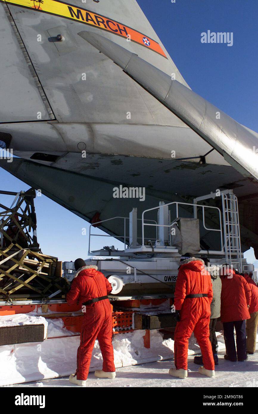 Loadmasters and civilian cargo workers guide a load onto a cargo sled ...