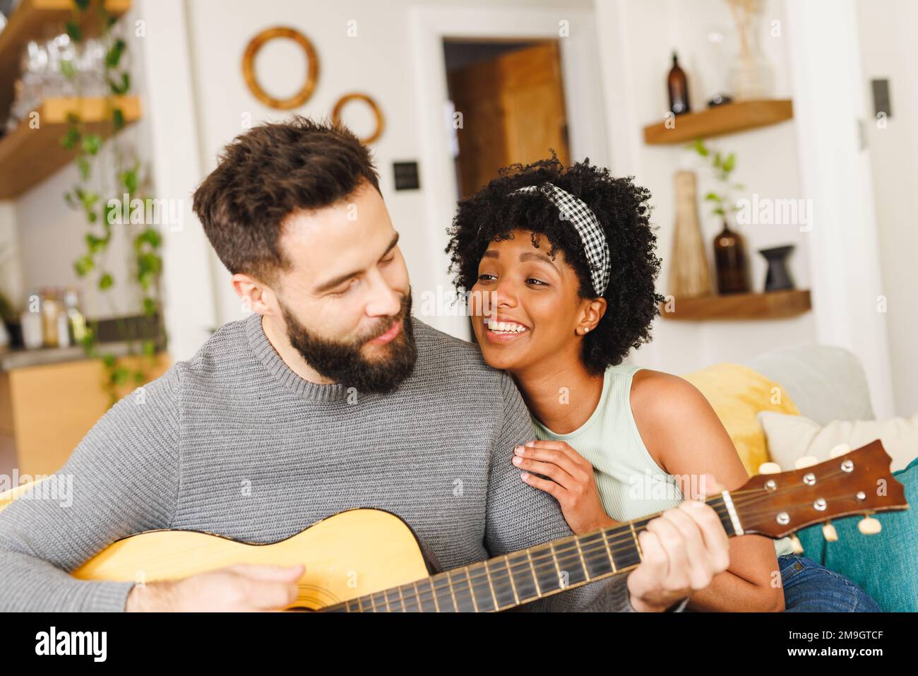 Smiling biracial young woman with afro hair embracing boyfriend singing ...