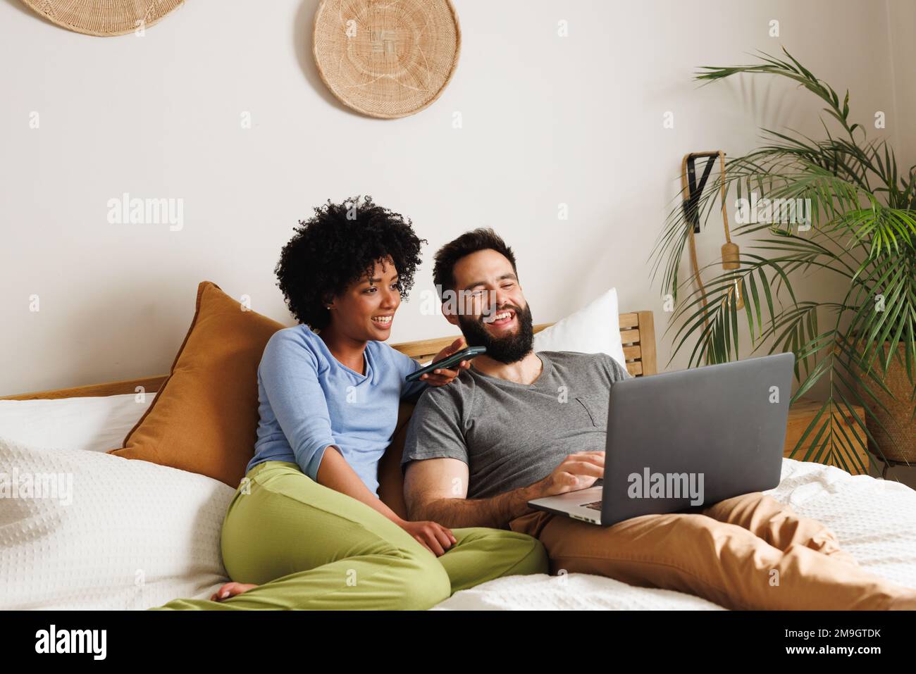Cheerful biracial young couple watching moving over laptop while ...
