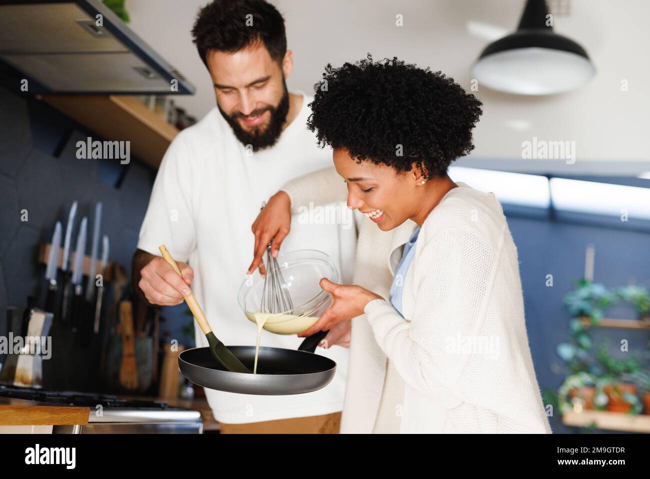 Happy biracial young couple pouring batter in cooking pan while making ...