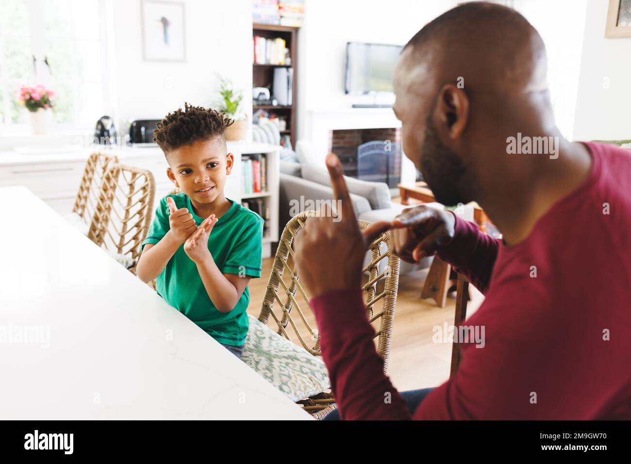 Happy african american father and son at table, talking in sign ...