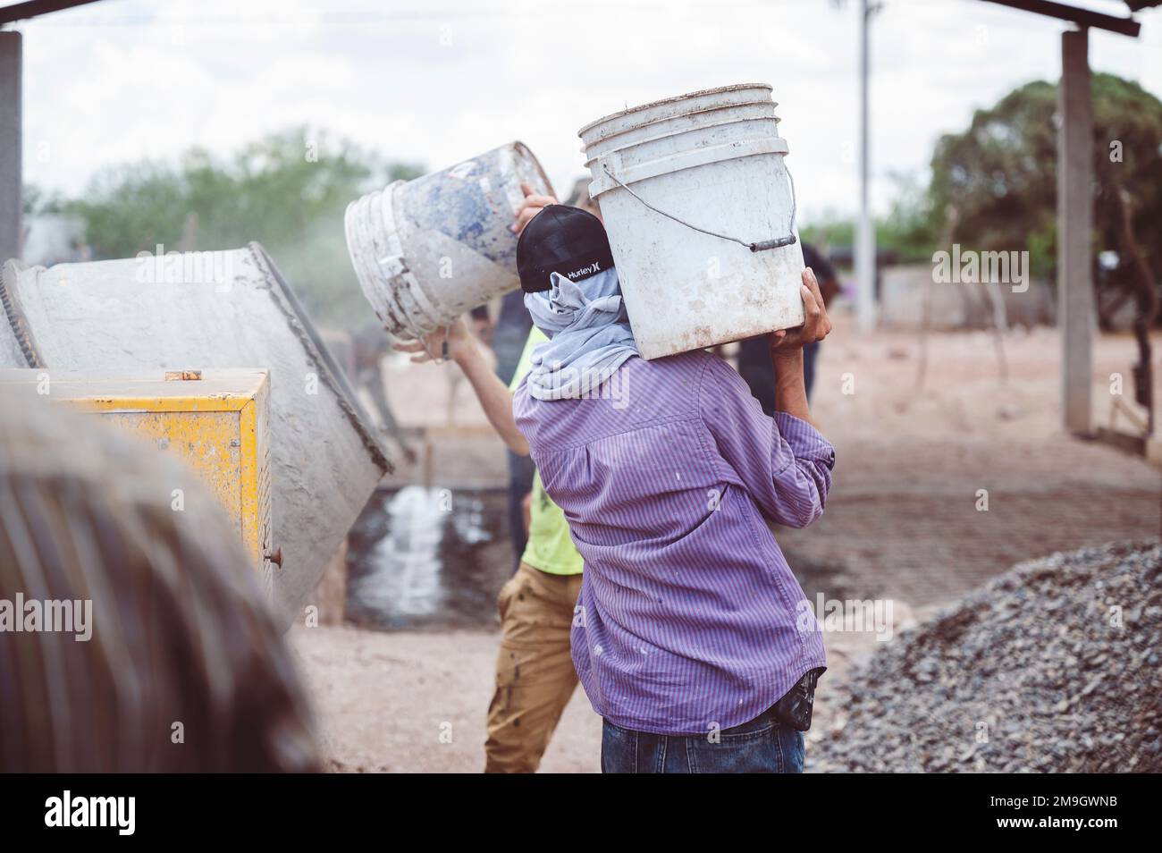 A group of workers, pouring gravel into a bucket and carrying it to a ...