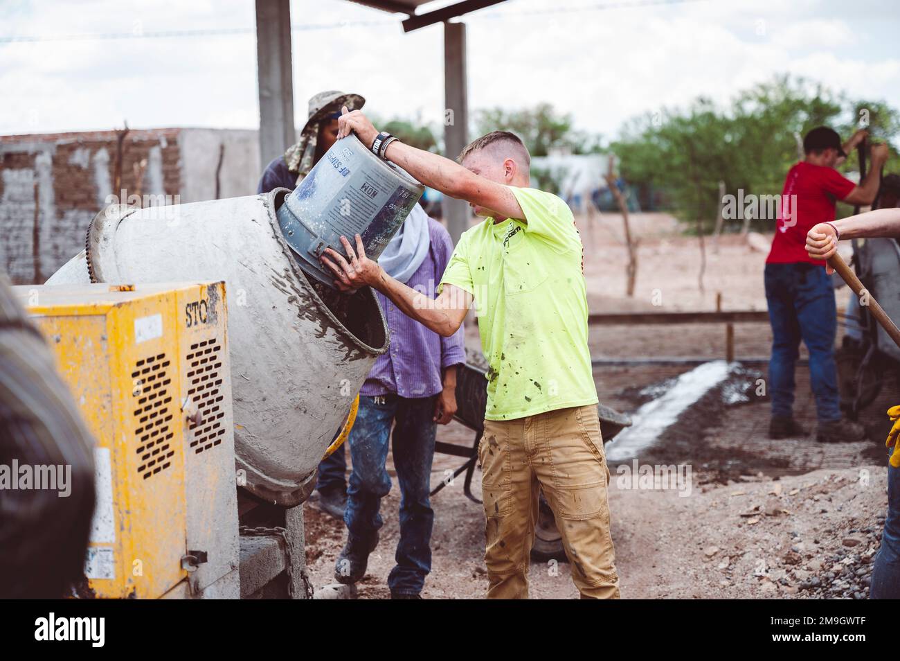 A group of workers, pouring gravel into a bucket and into a concrete ...