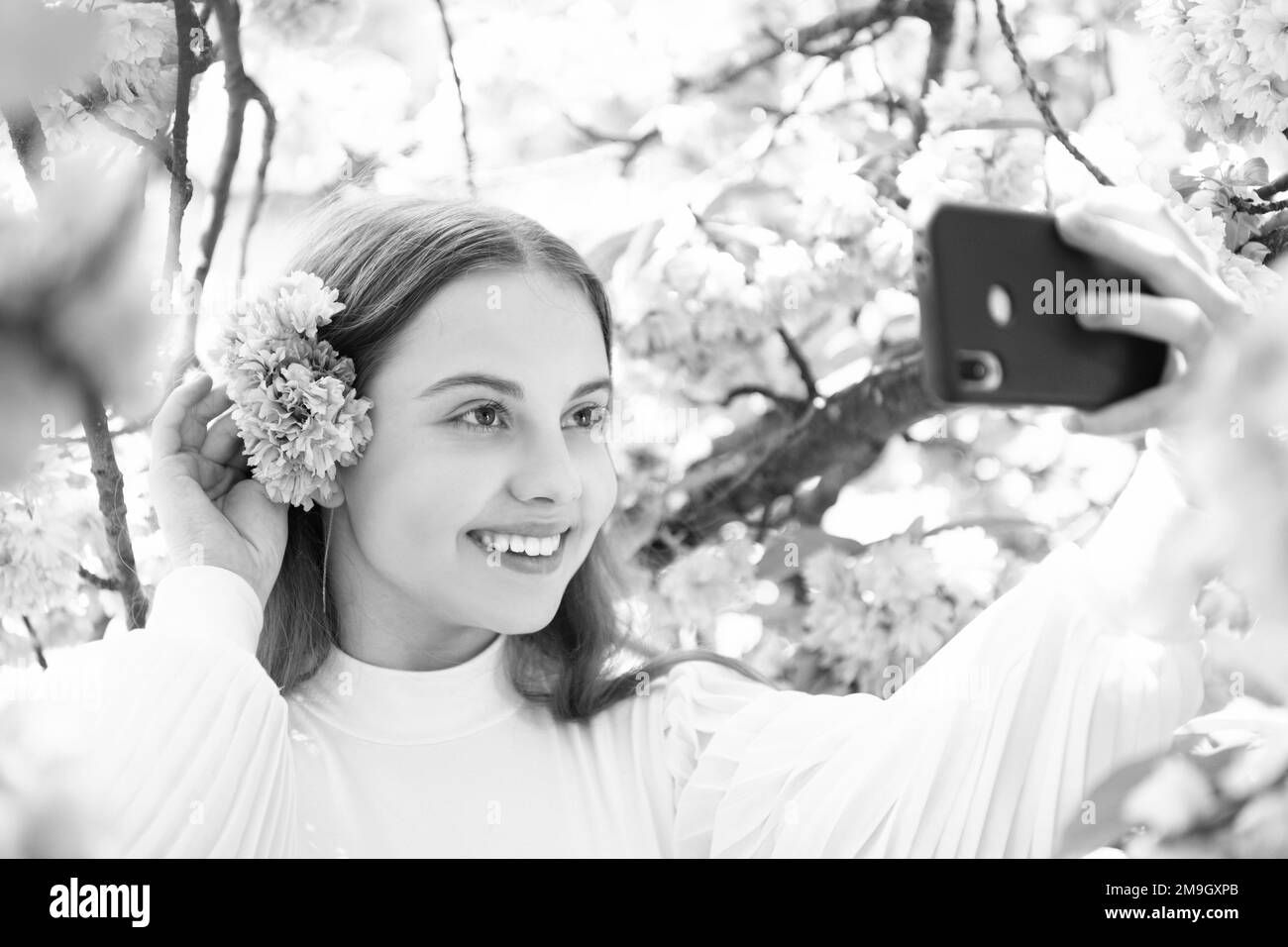 Portrait of happy girl taking selfie at flowering sakura tree in spring ...