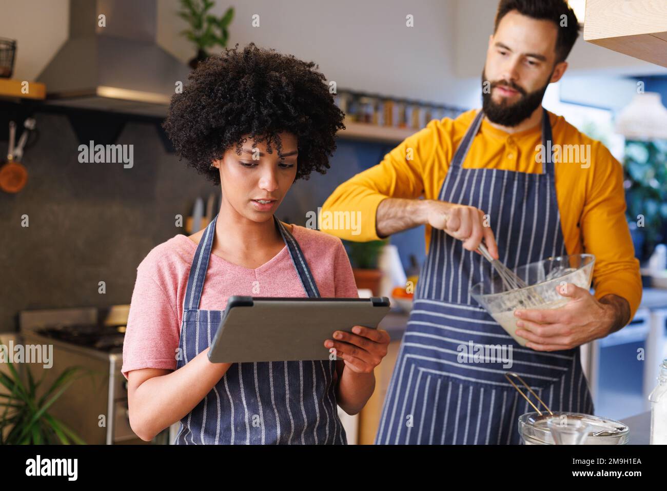 Biracial young woman watching recipe on digital tablet while boyfriend ...