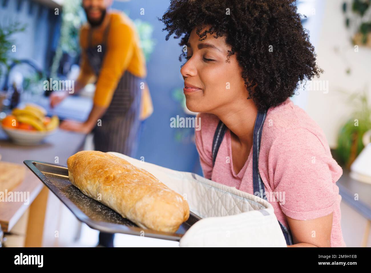 Biracial woman with eyes closed smelling freshly baked loaf of bread ...