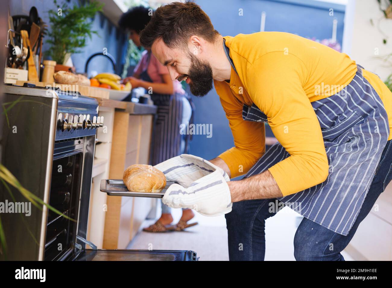 Biracial bearded man removing freshly baked loaf of bread from oven ...