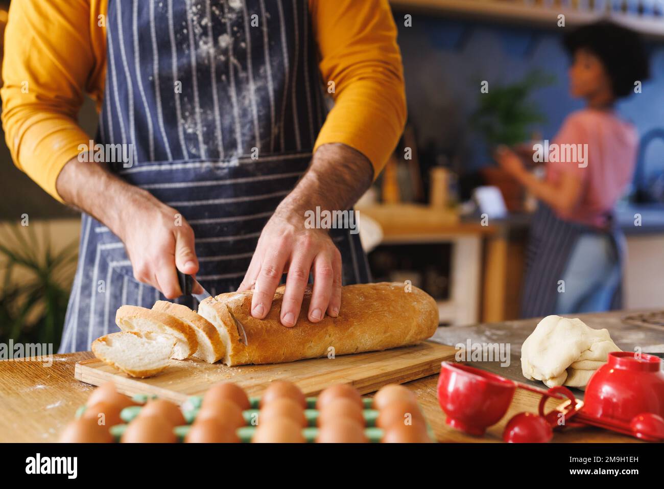 Midsection of biracial man cutting loaf of bread into slices on table ...
