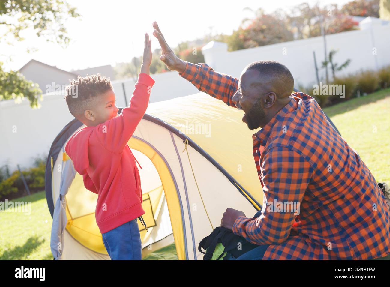 Happy african american father and son high-fiving in their backyard ...