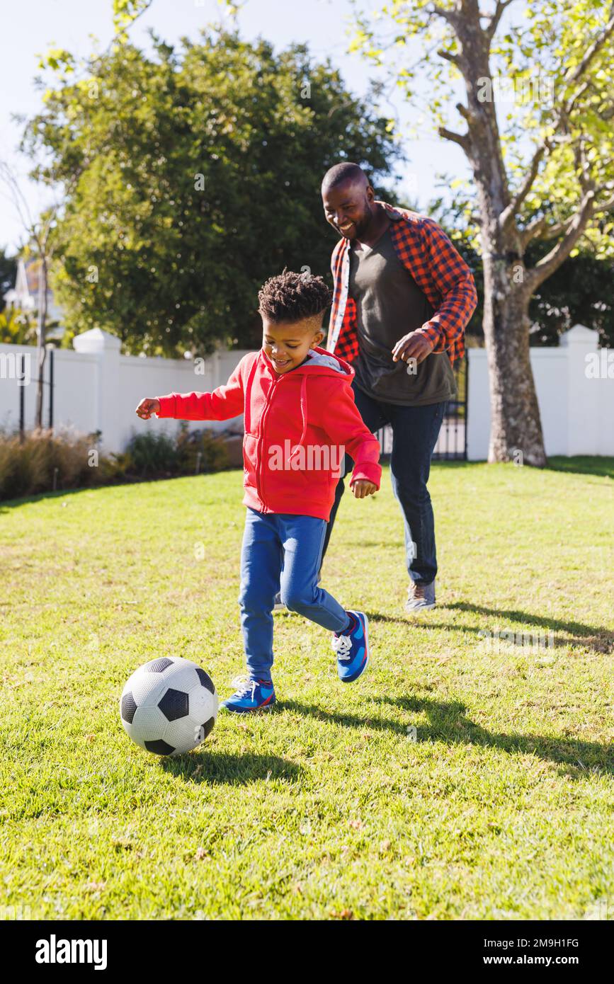 Happy african american father and son playing football in their ...