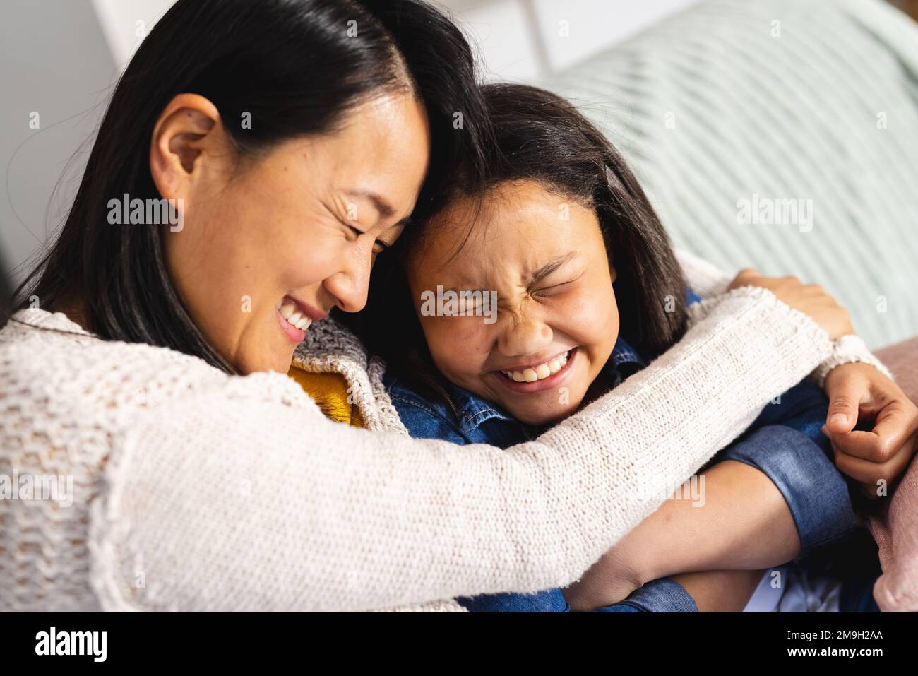 Happy asian mother and daughter sitting on sofa in living room and embracing Stock Photo - Alamy