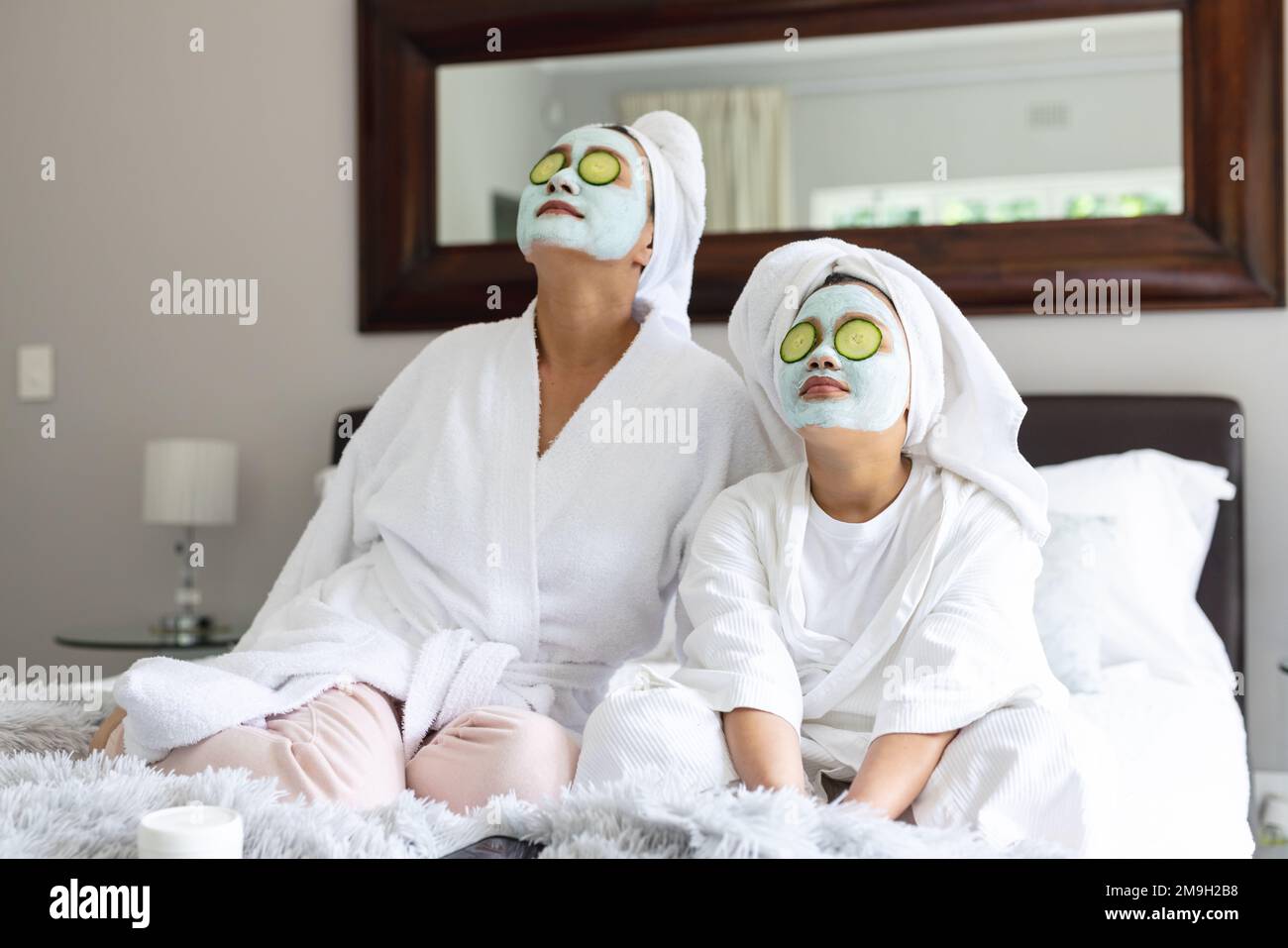 Happy asian mother and daughter sitting on bed and wearing beauty face ...