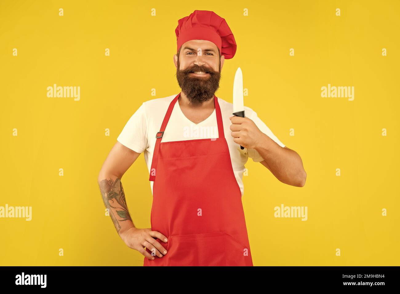 Happy man in red apron and toque holding chefs knife yellow background ...