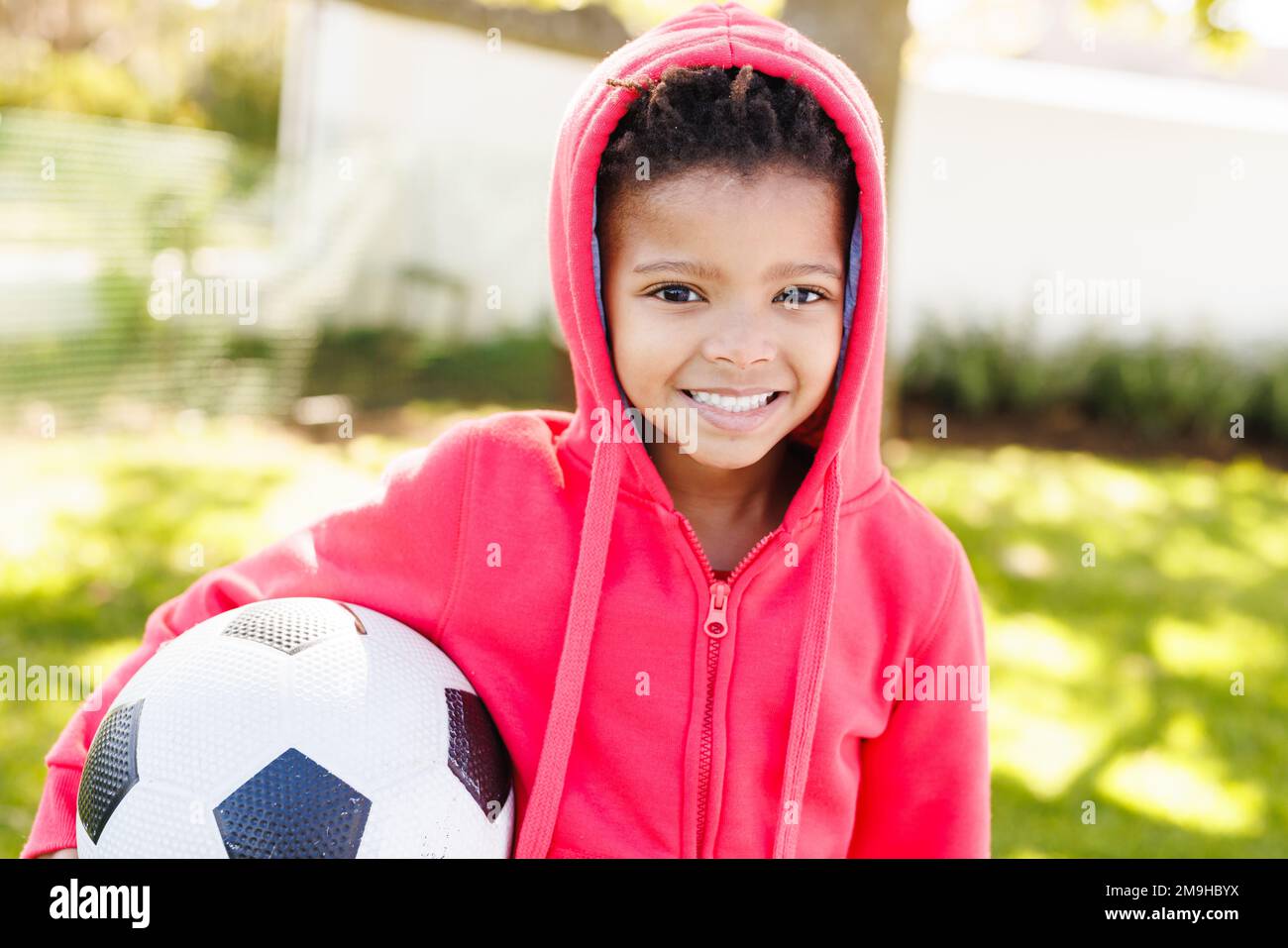 Portrait of happy african american boy holding football in backyard ...