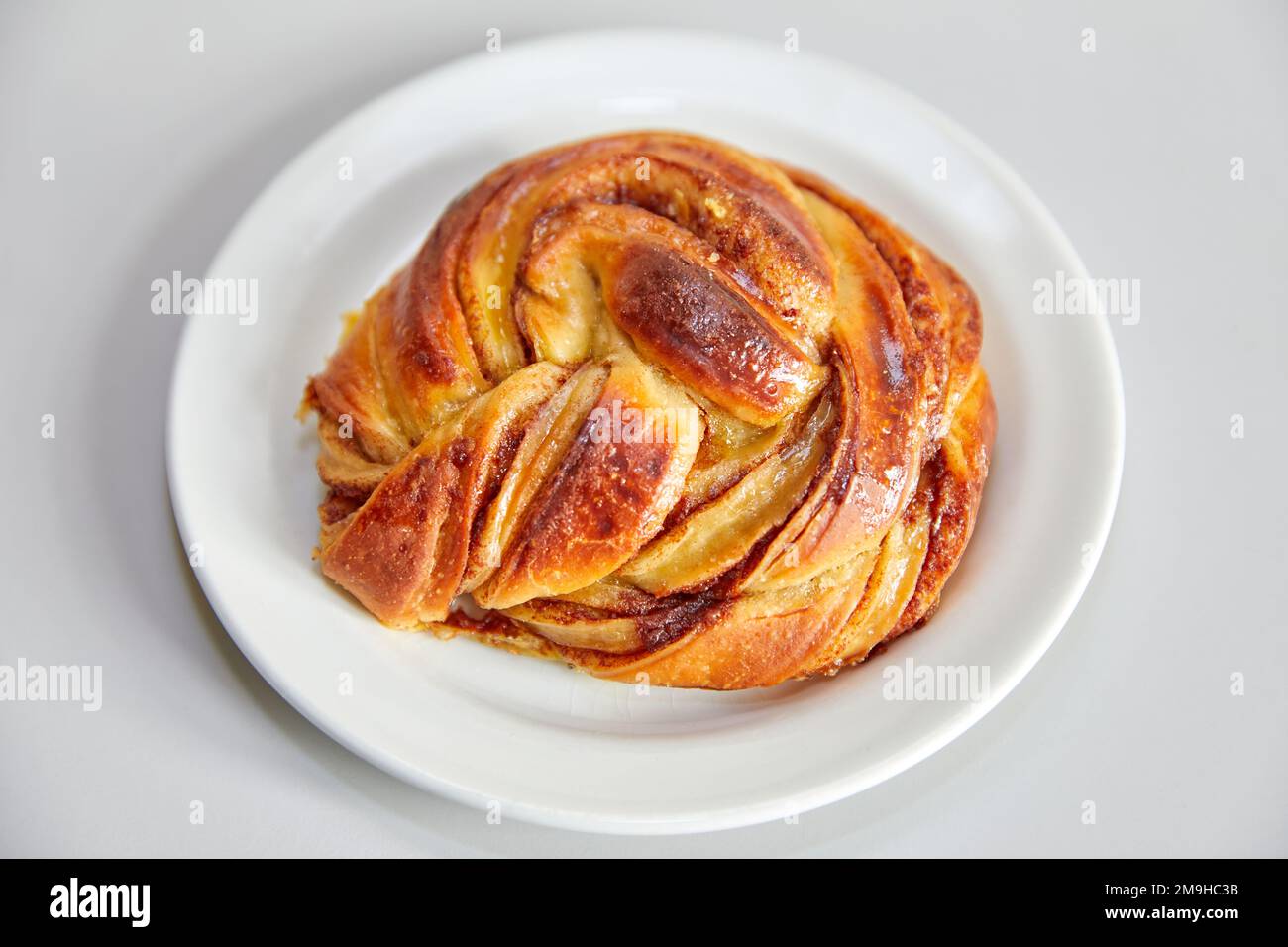 Danish cinnamon bun on a white plate Stock Photo - Alamy