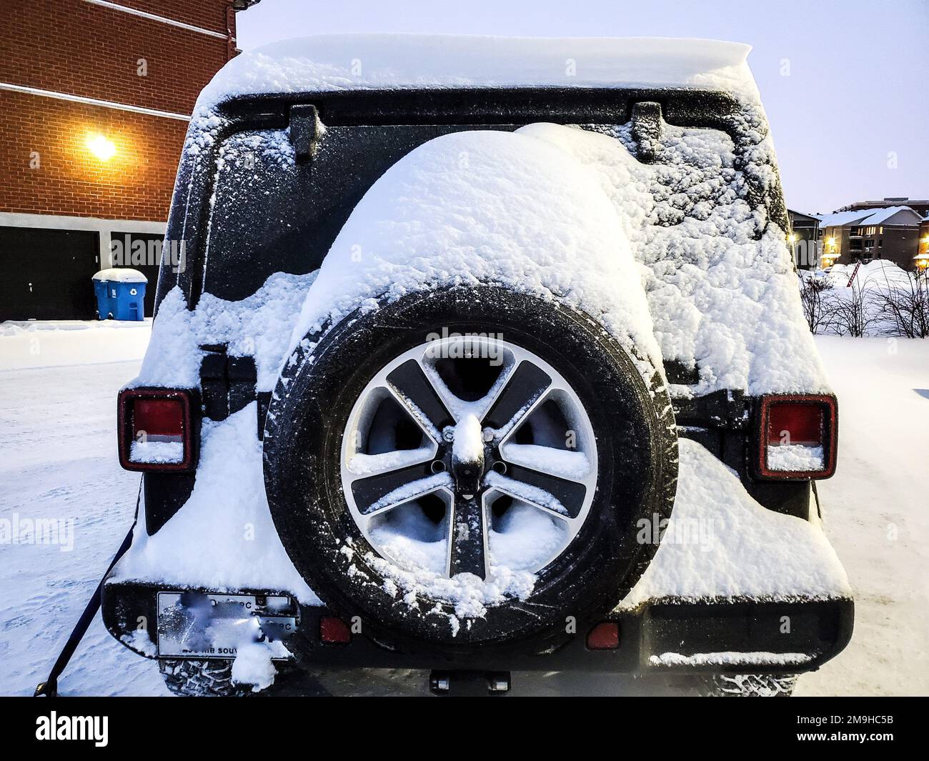 A closeup view of a modern black car covered in white snow in winter ...