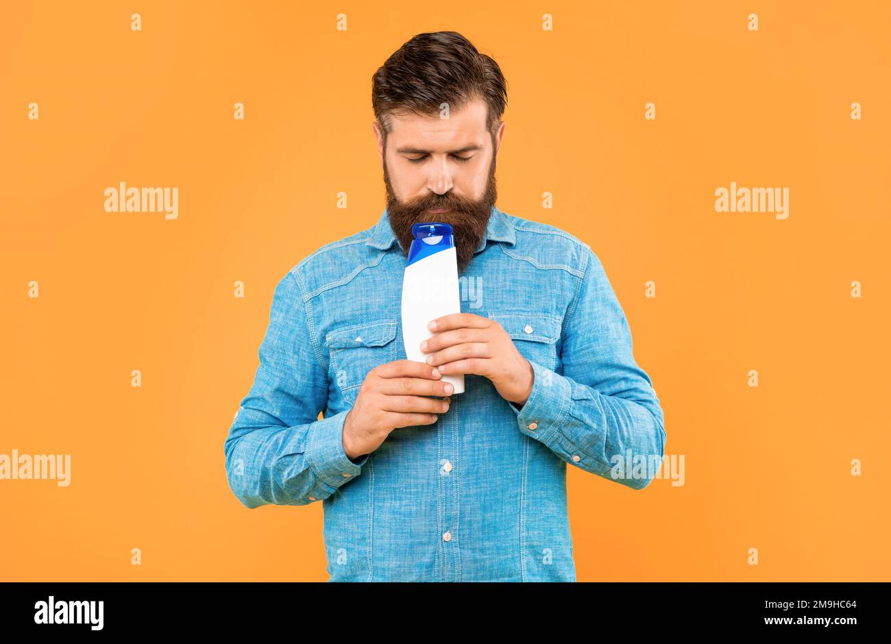 brutal bearded man smelling shampoo bottle on yellow background ...