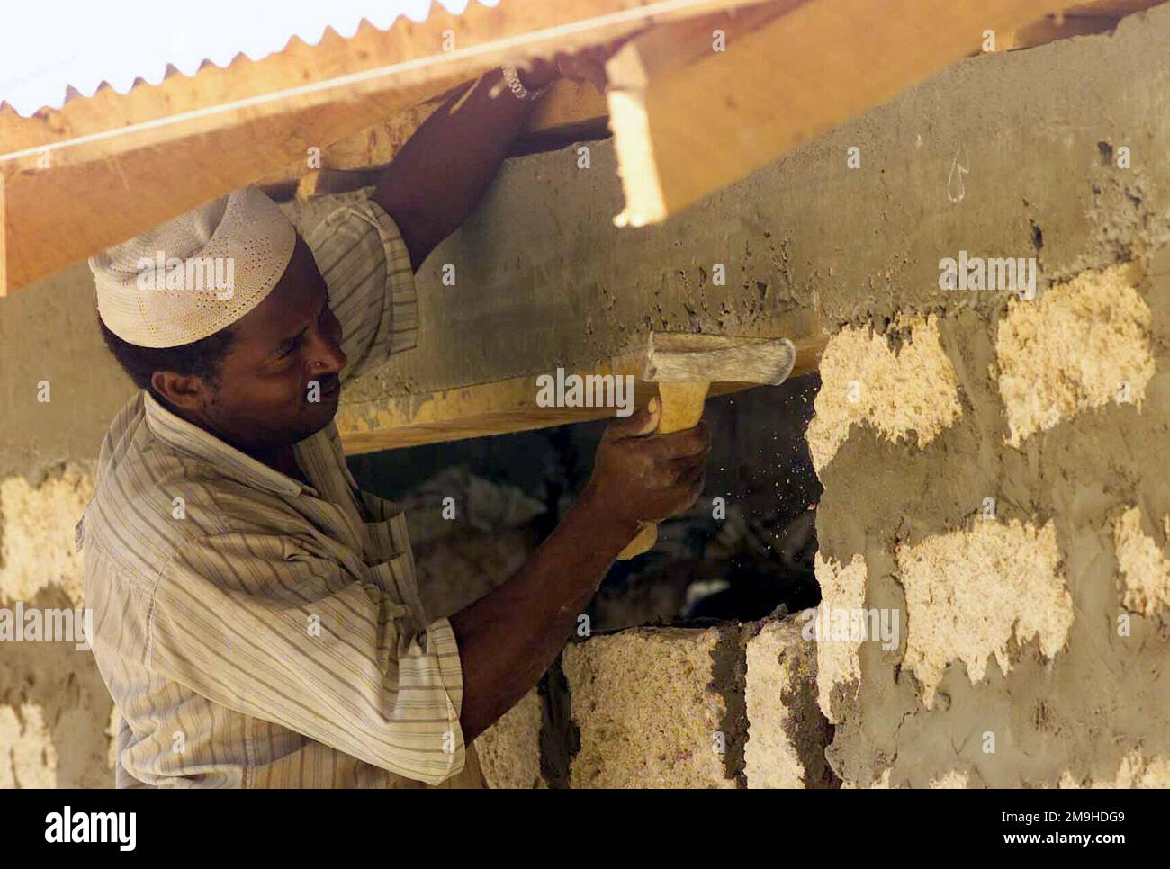 A local Kenyan construction worker trims some of the Coral brick with ...