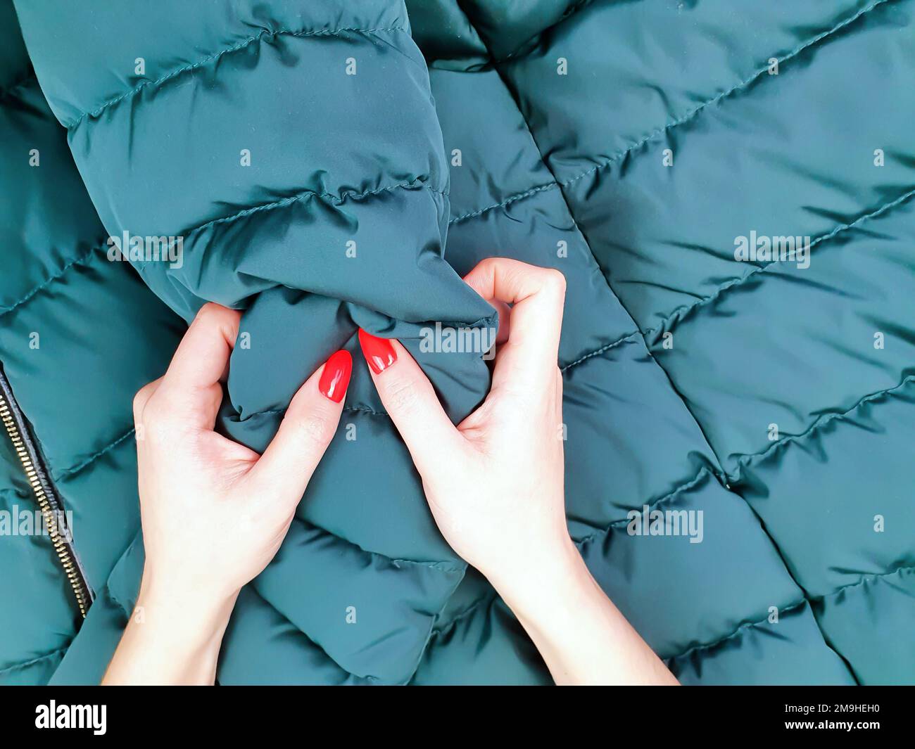 Young woman testing green puffer jacket textile. Female hands with red ...