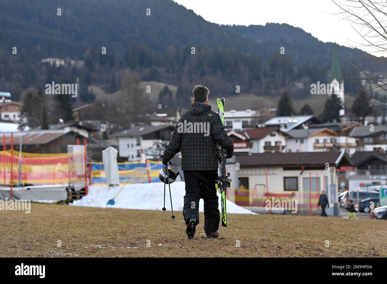 A skier carries his skis and walks on foot across a brown meadow ...