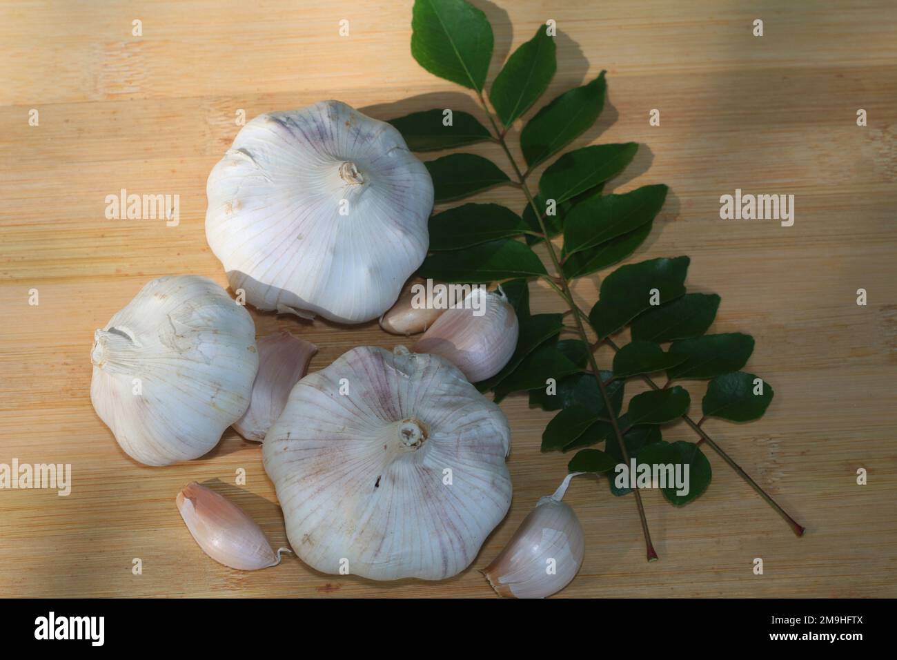 A closeup of garlic and a curry leaf isolated on a wooden cutting board ...