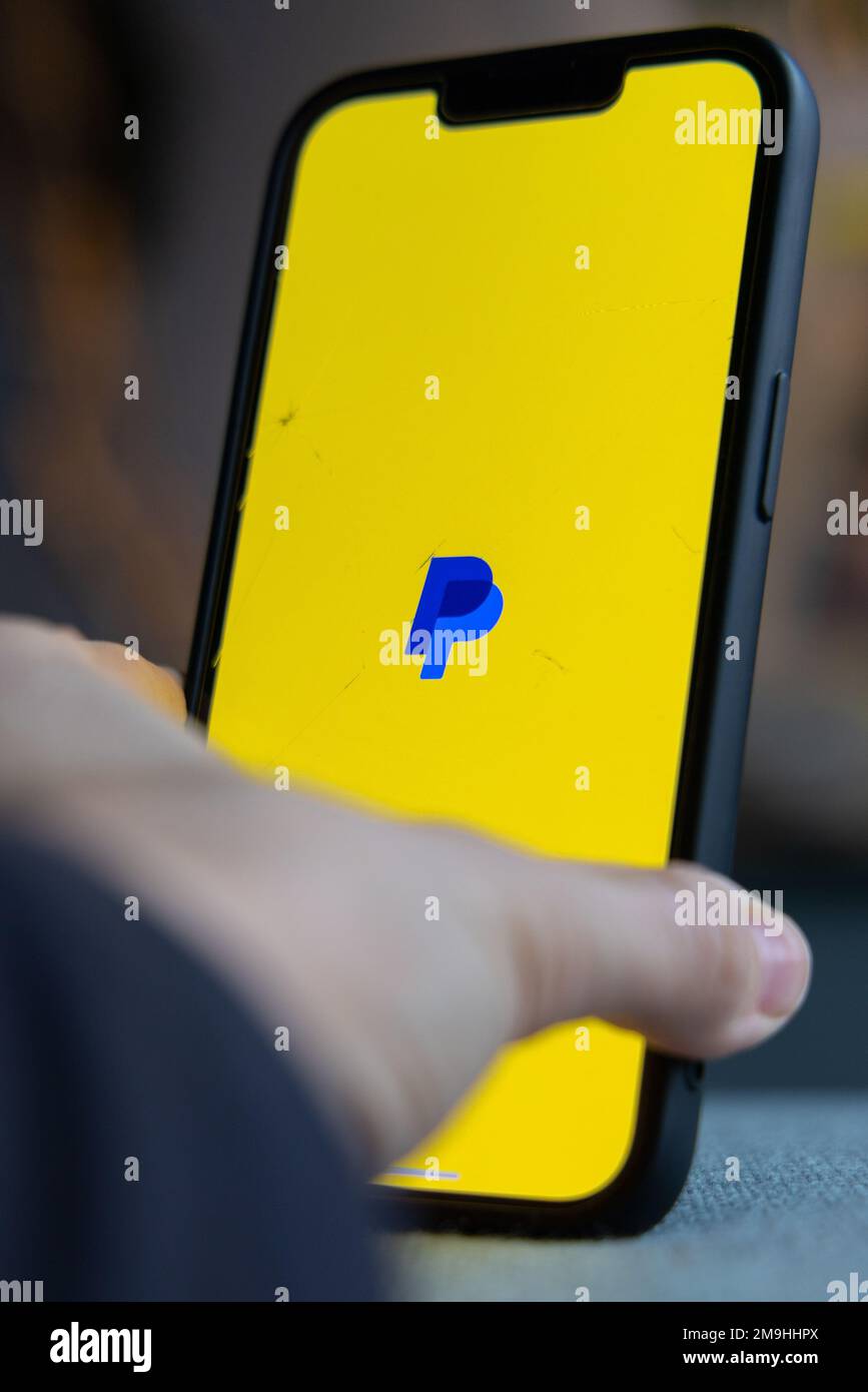 Hand holding a smartphone with PayPal icon on screen. Blue pay pal logo ...