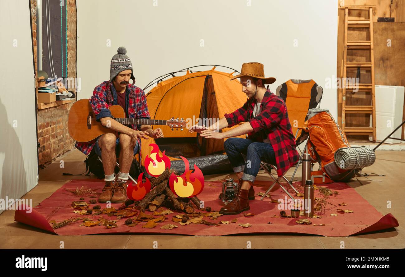 Warming hands over fake fire. Two men imagining, recreating camping ...