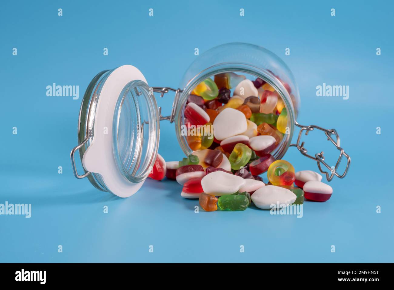 candy sweet glass jar opened with candy sweets poured on light blue ...