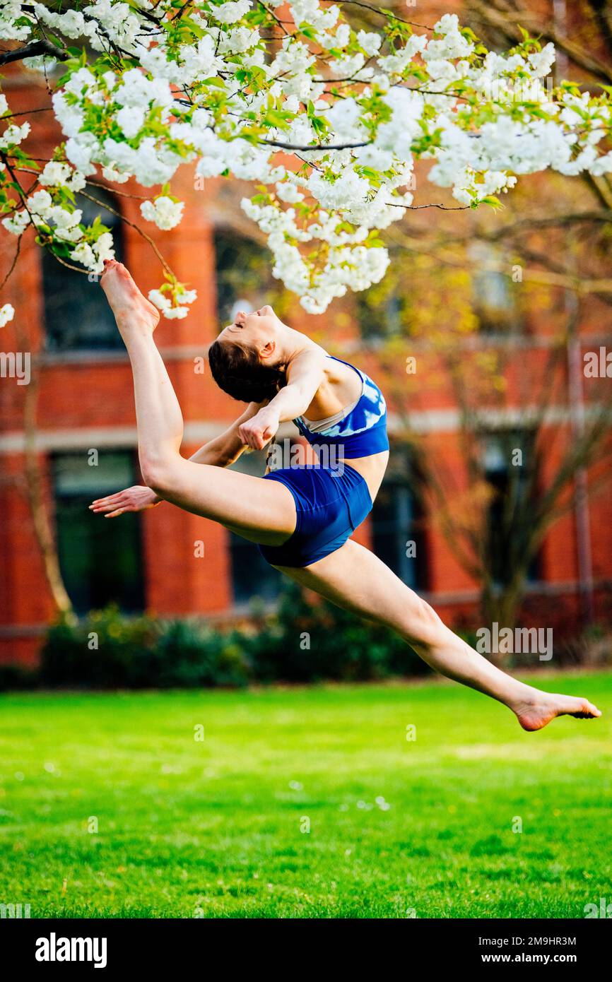 Acrobat in blue clothing jumping under cherry blossom in park ...