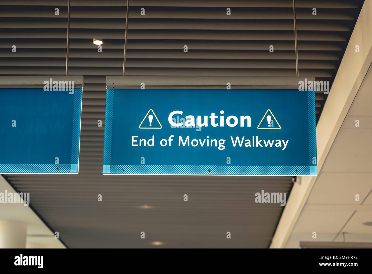 A hanging blue cation sign warning the end of a moving walkway Stock ...