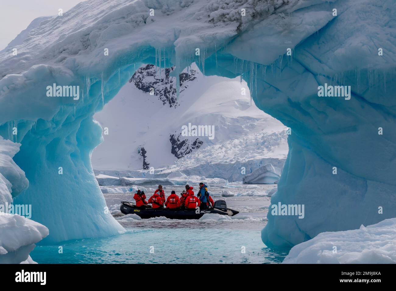 Tourists in a zodiac exploring an iceberg arch in Cierva Cove, a cove ...