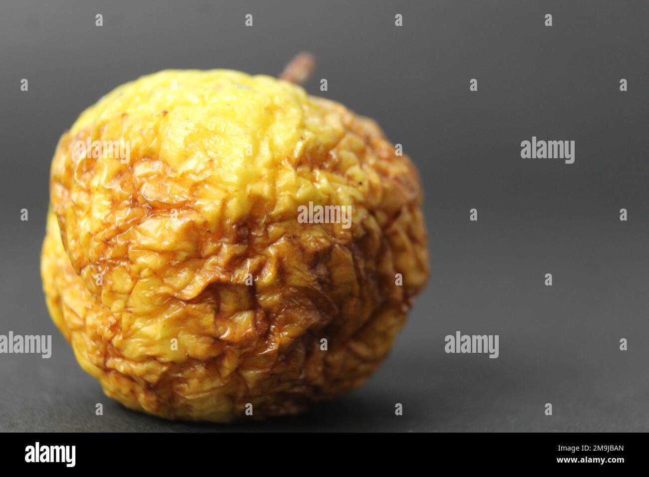 a dry old apple wrinkled on a black background. Ugly foods. Bad spoiled ...