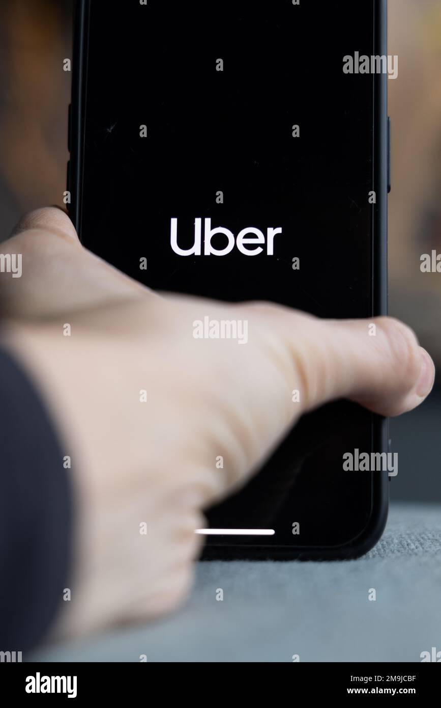 Hand holding a smartphone with Uber icon on screen. White Uber on black ...