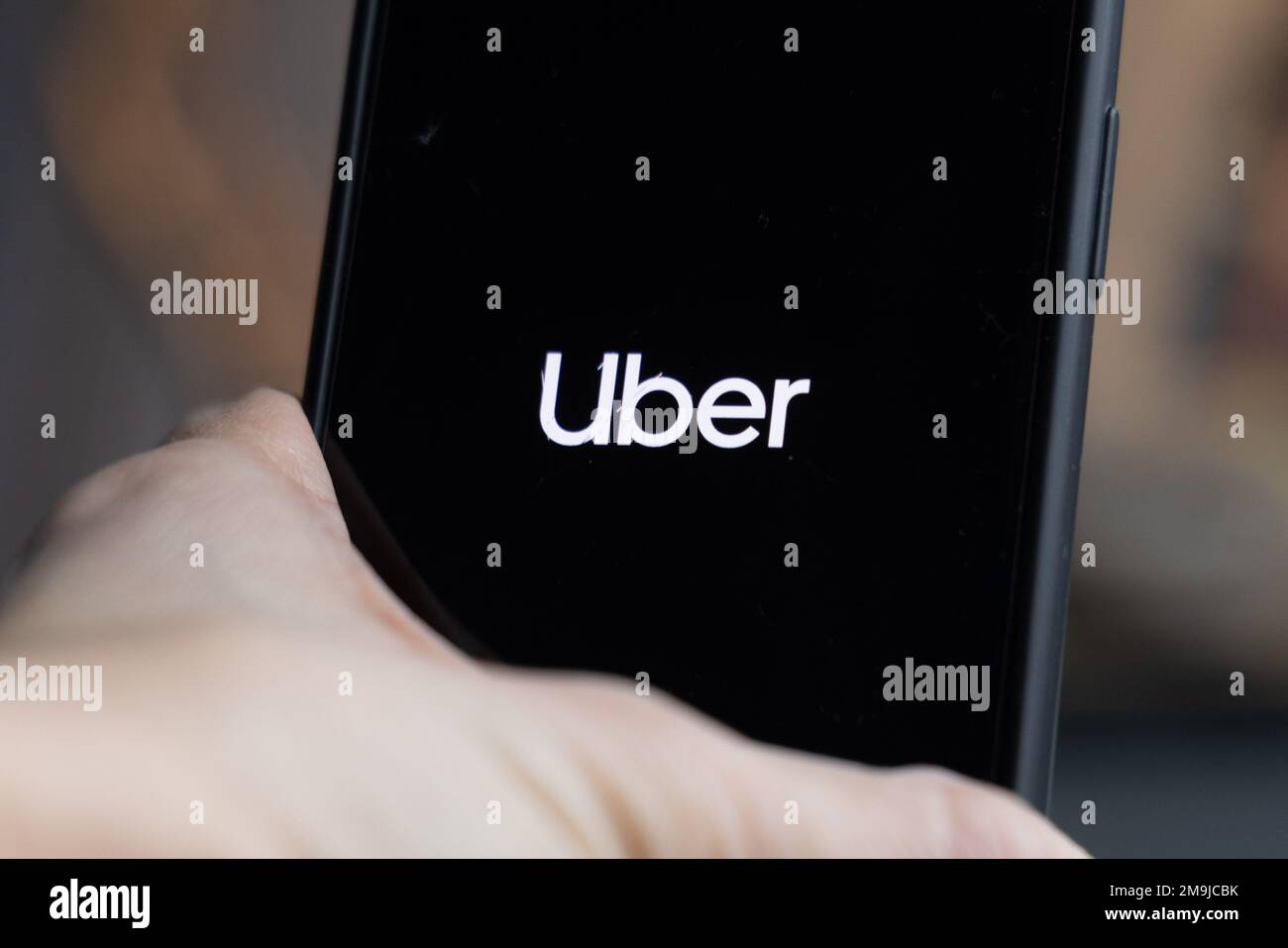 Hand holding a smartphone with Uber icon on screen. White Uber on black ...