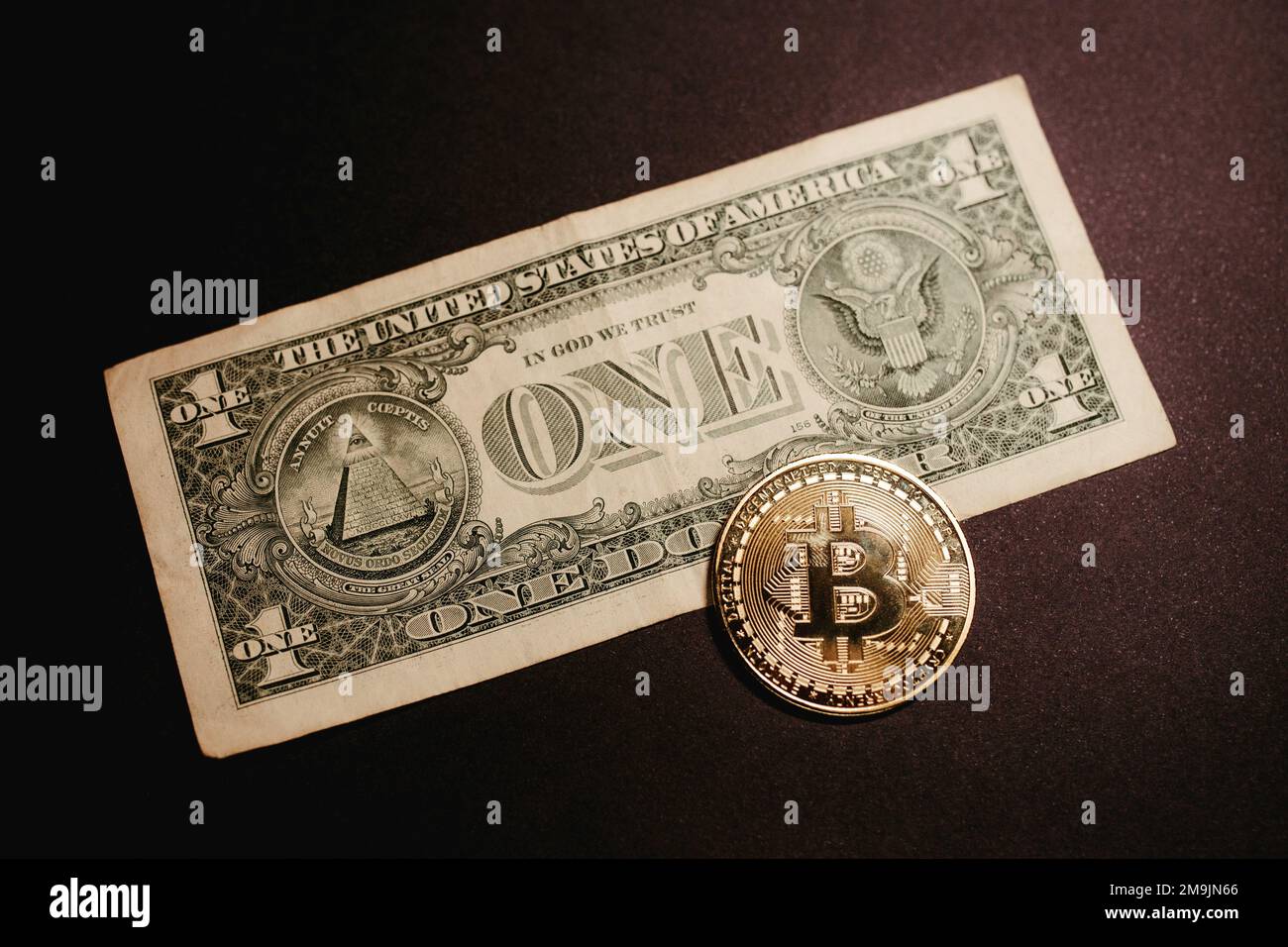 A closeup shot of a Bitcoin lying on a one-dollar bill on a black ...