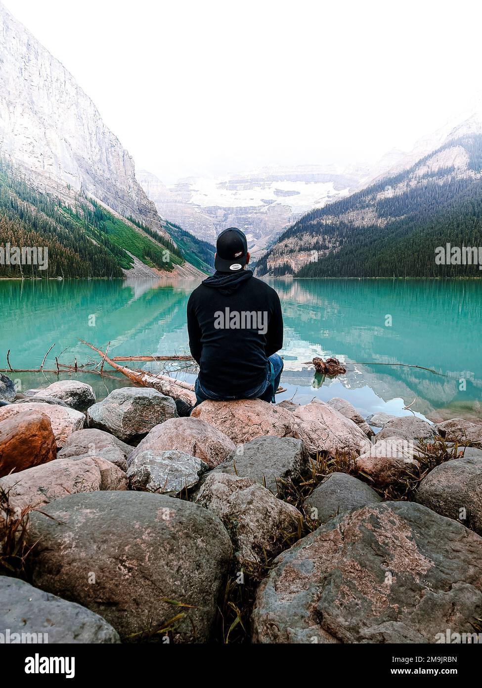 a tourist sitting on rocks and facing peaks and water Stock Photo - Alamy