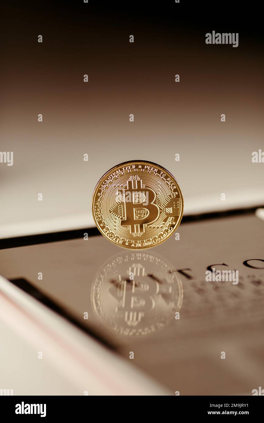 A vertical shot of a Bitcoin lying on a newspaper about cash system ...