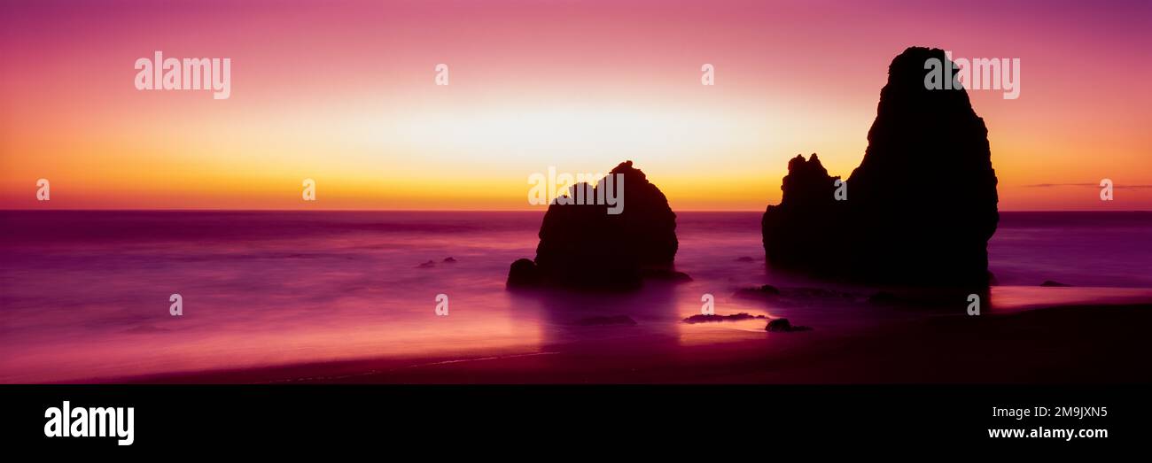Silhouettes of rock formations on beach at sunset Stock Photo - Alamy